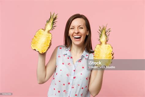 스튜디오에서 분홍색 파스텔 벽 배경에 고립 된 신선한 잘 익은 파인애플 과일의 Halfs를 들고 여름 옷에 젊은 여자를 웃 고 사람들은 생생한 라이프 스타일 휴식 휴가