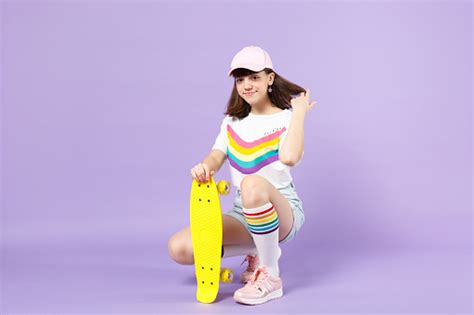 생생한 옷에 아름 다운 십 대 소녀 앉아 노란색 스케이트 보드 스튜디오에서 보라색 파스텔 벽 배경에 고립 된 찾고 카메라 사람들은 진심으로 감정 라이프 스타일 개념입니다