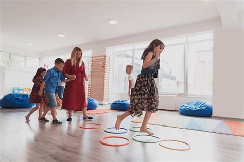 작은 보육원 아이들 교실에서 실내 바닥에 여성 교사와 함께 운동을하고 훌라 후프 서클을 뛰어 넘으면 바닥에서 추적됩니다 체육에 대한 스톡 사진 및 기타 이미지 Istock