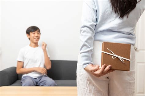 젊은 아시아 여성은 거실의 소파에 앉아있는 남자 놀람과 함께 선물 상자를 숨 깁니다 12 13세에 대한 스톡 사진 및 기타 이미지 12 13세 25 29세 2명