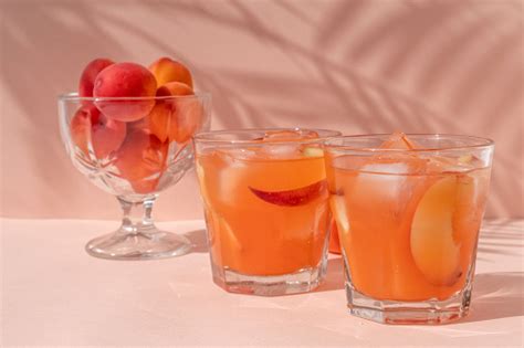 복숭아 과일 아이스 상쾌한 주스 또는 칵테일 음료가 담긴 두 잔 열대 햇빛 그림자가 있는 밝은 복숭아 분홍색 배경에 복숭아와