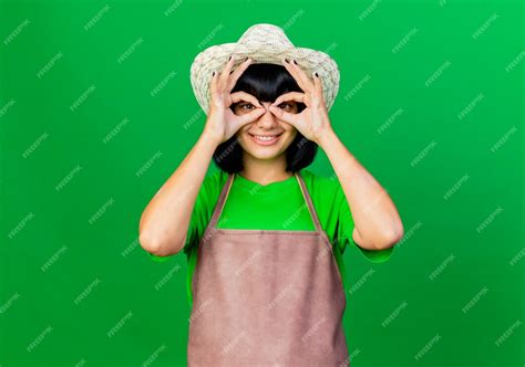 원예 모자를 쓰고 제복을 입은 웃는 젊은 여성 정원사 무료 사진