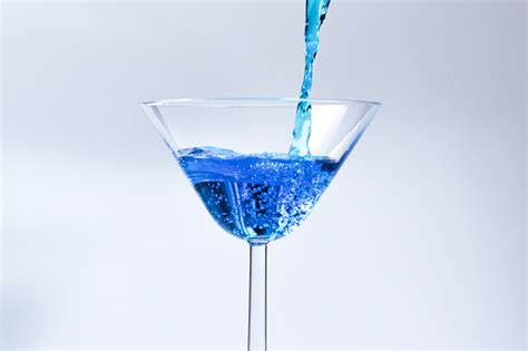 유리에 푸른 액체와 칵테일 물튀김과 방울로 액체를 붓는 푸른 물이있는 유리 흰색 배경에 스플래시와 알코올로 채우는 마티니 유리 상쾌한 음료 컨셉 0명에 대한 스톡 사진 및