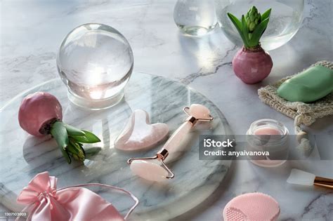 대리석 돌 배경에 과샤 마사지기와 핑크 쿼츠 얼굴 롤러 페이스 케어 제품 유리 크리스탈 볼과 이국적인 야자수 잎 수건 보습 크림 스킨케어 강장제 에센셜 오일 세럼 구에 대한