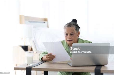 종이 문서를 찾고 집에서 노트북 컴퓨터를 사용하는 고위 여성 60 64세에 대한 스톡 사진 및 기타 이미지 60 64세 가정 생활 가정의 방 Istock
