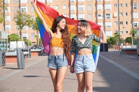 Young Lesbian Couple Smiling Holding Hands And Walking With A Rainbow