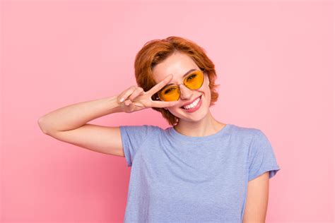 그녀의 그녀의 좋은 귀여운 매력적인 매력적인 사랑 스러운 윈 섬 달콤한 쾌활 한 소녀를 입고 캐주얼 블루 티셔츠 노란 안경을 보여주는 V기호 근처 눈 분홍색 파스텔 배경