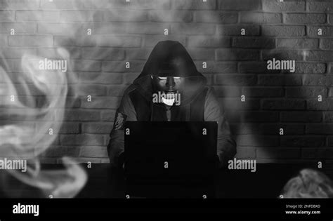 Hacker In Black Mask And Hood At The Table In Front Of The Monitor Stock Photo Alamy