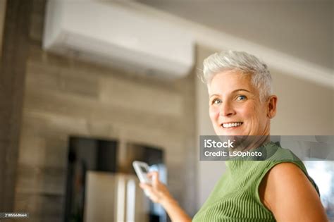 리모컨을 들고 벽에 설치된 에어컨의 온도를 조절하는 여자 Indooor 쾌적한 온도 50 59세에 대한 스톡 사진 및 기타 이미지 50 59세 55 59세 가습기