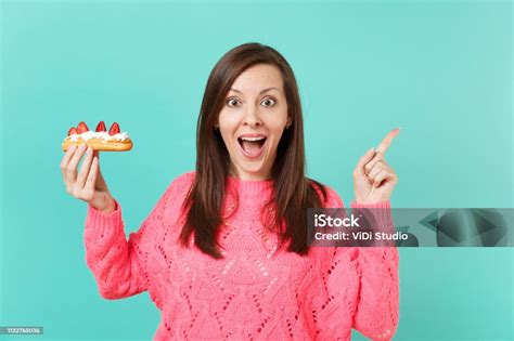 활짝 열려 입 넓은 니트 핑크 스웨터에 놀란 젊은 여자 포인트 인덱스 손가락이 옆으로 잡고 파란색 벽 배경에 고립 된 손에 클레어 케이크 사람들 라이프 스타일 개념입니다