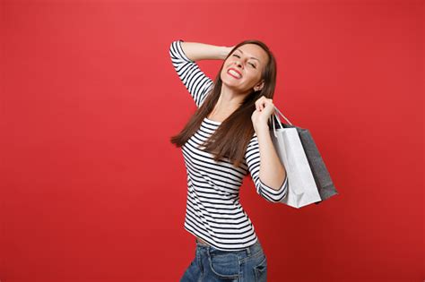 줄무늬 옷 빨간 벽 배경에 고립 쇼핑 후 구매와 패키지 가방을 들고 아름 다운 젊은 여자의 초상화 사람들이 진심으 감정 라이프 스타일 개념 복사 공간을 비웃는 다 갈색