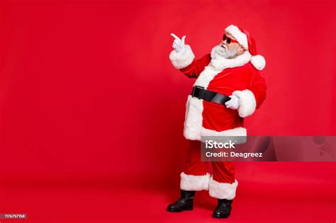 빨간 배경 위에 고립 된 밝은 의상 벨트를 착용 프로모션을 보여주는 안경 안경에 매력적인 산타 클로스의 전체 길이 프로필 측면