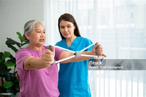 물리 치료 센터에서 팔 근육 회복을 위한 젊은 물리치료사와 함께 고무 확장기로 운동하는 행복한 노인 여성 간병인과 건강의