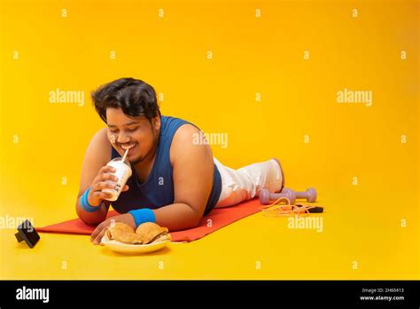 A Fat Man Lying On Yoga Mat Drinking Drink With A Plate Of Burger