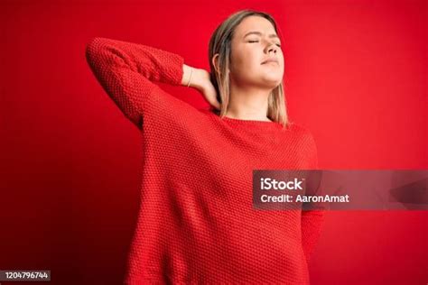 젊은 아름 다운 금발 여자 입고 캐주얼 스웨터 위에 빨간 고립 된 배경 목 통증 부상 손으로 목을 만지는 근육 통 건강관리와