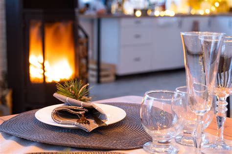 크리스마스와 새해를 위해 장식 된 로프트 하우스 내부의 스토브 벽난로 근처에서 접시 포크 나이프 냅킨 안경이있는 축제 테이블을 제공합니다 축제 저녁 식사를 위해 손님을