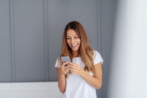 침실과 스마트 폰을 사용 하 여 서 있는 잠 옷에 아름 다운 웃는 백인 갈색 머리 아침 루틴 Brand Name Online Messaging Platform에 대한 스톡