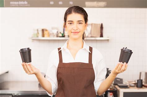 아름다운 백인 바리스타 여성이 팔을 펼치고 커피 바에서 두 손에 테이크 아웃 커피 컵을 보여줍니다 25 29세에 대한 스톡 사진