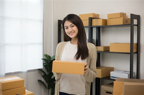 아름다운 젊은 아시아 기업가 서 포즈 카메라에 미소 집에서 일하는 상자가있는 여성 중소기업 소유자 배경에 많은 소포를 가진 시작
