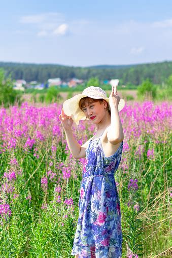 더운 여름날 초록색 숲과 푸른 하늘을 배경으로 밀짚 모자를 쓴 꽃밭에 있는 젊은 여성 개화기에 대한 스톡 사진 및 기타 이미지 개화기 걷기 꽃 식물 Istock