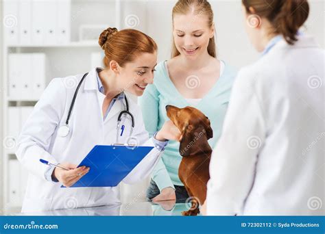 Счастливая женщина с собакой и доктором на клинике ветеринара Стоковое Фото изображение