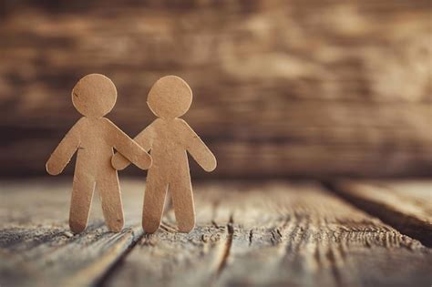 Two Paper Cutout Figures Holding Hands On Wooden Surface Friendship Unity And Support Concept
