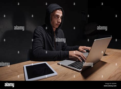 Hacker In Black Hoodie Using Laptops At Tabletop With Tablet In Dark