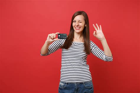 깜박이 밝은 빨간 벽 배경에 고립 된 신용 카드를 들고 보여주는 확인 서명 줄무늬 옷에 쾌활 한 젊은 여자의 초상화 사람들이 진심으 감정 라이프 스타일 개념 복사 공간을