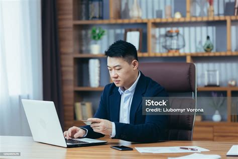 성공적인 아시아 사업가는 은행 업무를 수행하고 전자 계좌에서 돈을 이체하고 노트북과 은행 신용 카드를 사용합니다 보기 정적