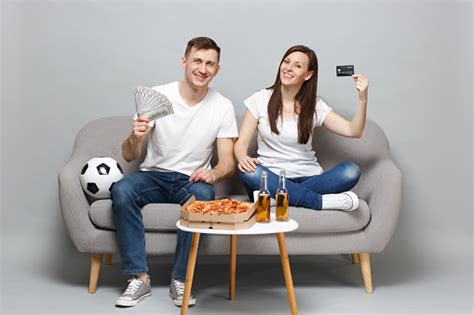 웃는 커플 여자 남자 축구 팬은 신용 카드를 들고 좋아하는 팀을 지원 합니다 달러 지폐에 돈의 팬 회색 배경에 고립 된 현금 돈 스포츠 가족 레저 라이프 스타일 개념입니다