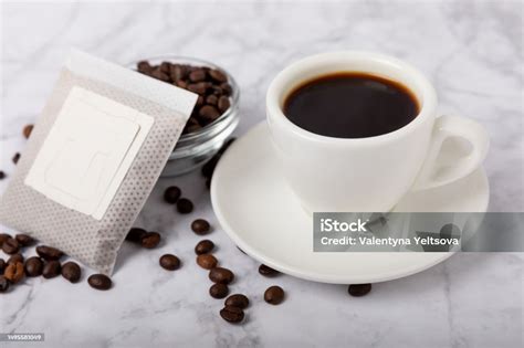 커피 백 커피 원두 흰색 컵을 텍스처 테이블에 떨어 뜨립니다 컵에 양조하기 위한 분쇄 커피 종이 봉지 드립 커피 필터 포장