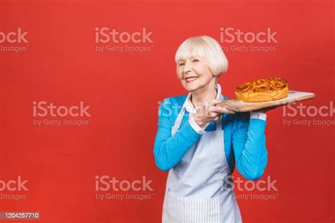 빨간 배경에 고립 된 달콤한 수제 파이 맛있는 롤빵을 보여주는 주름이있는 예쁜 매력적인 쾌활한 노인 여성의 초상화 집의 전문 가정 생활에 대한 스톡 사진 및 기타 이미지
