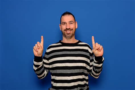 파란색 배경 스튜디오 초상화에 고립 된 포즈를 취한 줄무늬 풀오버에서 흥분한 수염을 가진 남자 사람들은 솔직한 감정 라이프 스타일 개념 모형 복사 공간 검지 손가락을 위로