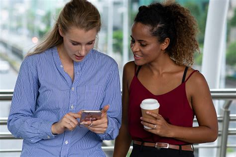 휴대 전화를 사용하여 웃는 흑인 여성과 이야기하고 도시 배경에 커피 한 잔을 들고 있는 백인 여성 도시에 대한 스톡 사진 및 기타 이미지 Istock