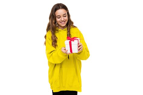 텍스트 에 대한 무료 공간과 흰색 배경에 고립 된 빨간색 리본흰색 상자에 선물을 들고 세련된 노란색 스포츠 후드에 아름다운 사랑스러운 긍정적 인 행복 미소 갈색 머리 십대