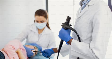 흰색 코트와 고무 장갑을 낀 아프리카 남자 의사가 현대 내시경으로 서서 젊은 여성 환자의 내시경 검사를 준비하는 자른 사진 사진