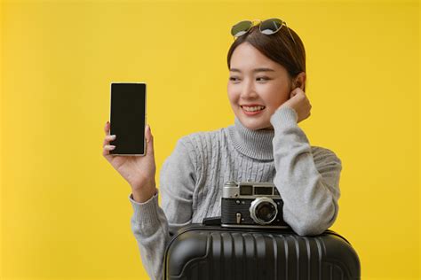 여성 아시아 관광객의 초상화 카메라와 수하물 회색 셔츠 노란색 배경에 고립 된 모바일 응용 프로그램을 제시하기위한 빈 템플릿 휴대 전화를 들고 30 34세에 대한 스톡 사진