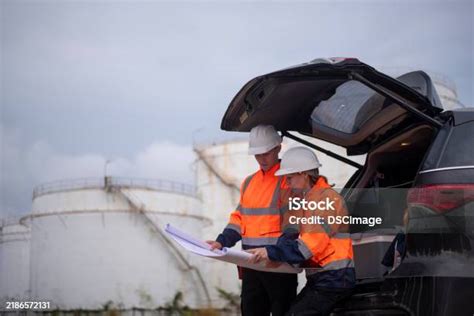안전모를 포함한 안전 장비를 착용한 엔지니어가 대형 청사진 태블릿을 조사하고 산업 시설에 서 있는 가스 또는 정유 공장에 종사하는 작업에 종사하는 높은 안전 기준 개념이