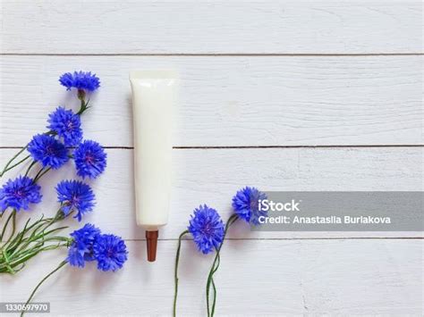긴 노즐과 청동 나사 캡과 나무 흰색 테이블에 파란색 야생 꽃과 아이보리 스퀴즈 화장품 튜브의 모형 브랜딩용 병 상단 보기 플랫레이 공간을 복사합니다 0명에 대한 스톡 사진