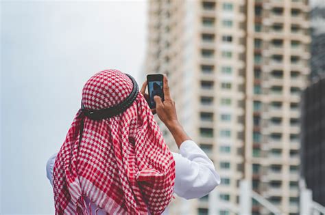 스마트 폰 응용 프로그램을 사용하는 이슬람 남자는 스마트 폰 무슬림 현대 아랍 도시를 들고 손에 일정 의제를 구성합니다 아랍 남성 착용 히잡과 무슬림 정장 드레스 보내는
