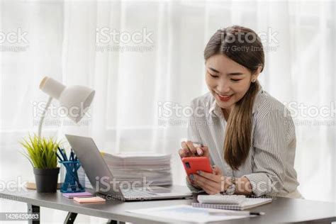 사무실 테이블에 재무 그래프를 분석하기 위해 노트북으로 작업하는 스마트 폰을 들고있는 매력적인 젊은 아시아 비즈니스 여성