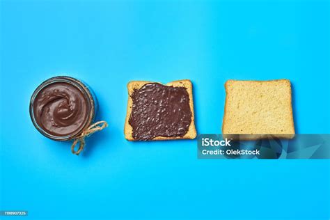 바닐라 빵 조각 근처에 녹은 초콜릿이 가득한 유리 항아리가 부엌의 파란색 책상 위에 놓여 있습니다 영양가있는 아침 식사 또는 점심 의 개념 맨 위 보기 가득 찬에 대한 스톡