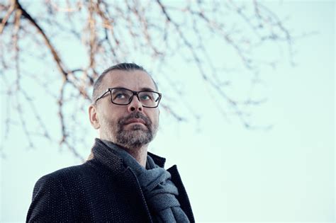 하늘을 배경으로 파란색 코트와 모직 스카프를 착용하고 안경을 쓴 자신감 넘치는 수염을 기른 중년 남성의 초상화 로우 앵글 뷰