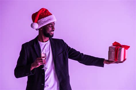 젊은 아프리카 젊은 남자 마시는 샴페인 과 들고 크리스마스 선물 고립 에 보라색 배경 12월에 대한 스톡 사진 및 기타 이미지