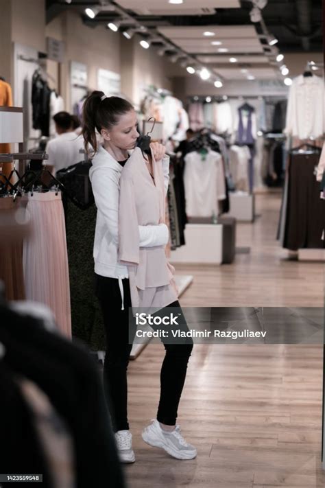 흰 옷을 입은 젊은 예쁜 여자가 부티크 매장 쇼핑 센터 거울 라이프 스타일 실생활 사진 의류 선택 새로운 컬렉션에서 치마를 입으려고합니다 고객에 대한 스톡 사진 및 기타
