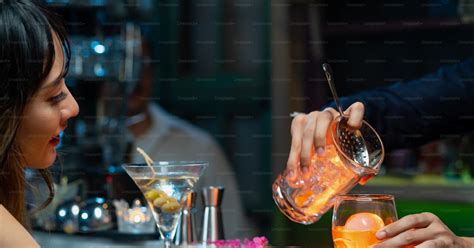 자신감 아시아 여성은 바 카운터에 앉아 알코올 음료를 마시고 나이트 클럽에서 바텐더와 이야기합니다 남성 믹솔로지스트 바텐더가 고객에게 알코올 음료를 준비하고 있다 소규모