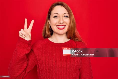 젊은 아름다운 빨간 머리 여자 와 스티커 프리젠 테이션 을 입고 안녕하세요 내 이름 메시지 승리 기호를하고 카메라에 윙크 행복한 얼굴미소 2번 긍정적인 감정 표현에 대한