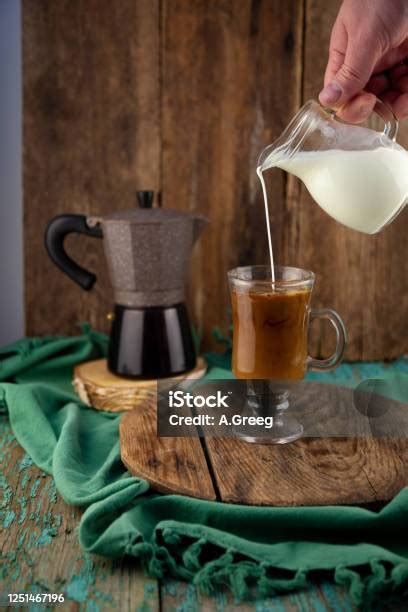 우유를 커피에 붓습니다 크림으로 커피를 만드세요 손에 유리 머리 카푸치노 한 잔 나무 테이블에 간헐천 커피 메이커 집에서 아침 식사를 요리하십시오 부엌 배경 카라페 크리머