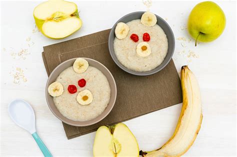 재미있는 귀여운 아이 아이들 아기의 건강한 아침 식사 점심 오트밀 죽 그릇에 사과 바나나 말린 베리 과일로 장식 된 곰 얼굴처럼