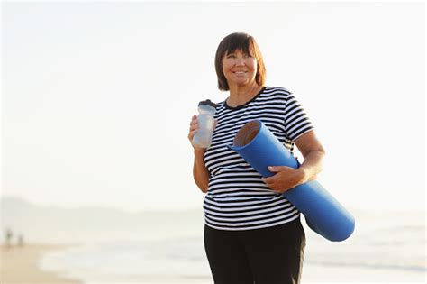 여름에는 바다로 해변에서 요가 매트를 들고 야외에서 운동을 한 후 물 한 병으로 성숙한 성인 여성을 웃고 있습니다 노인 건강한 라이프 스타일 활력 건강 관리 개념 복사 공간